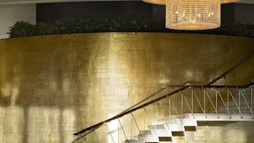 Um lustre imponente, uma escadaria de mármore e um espelho d'água em um hall moderno.