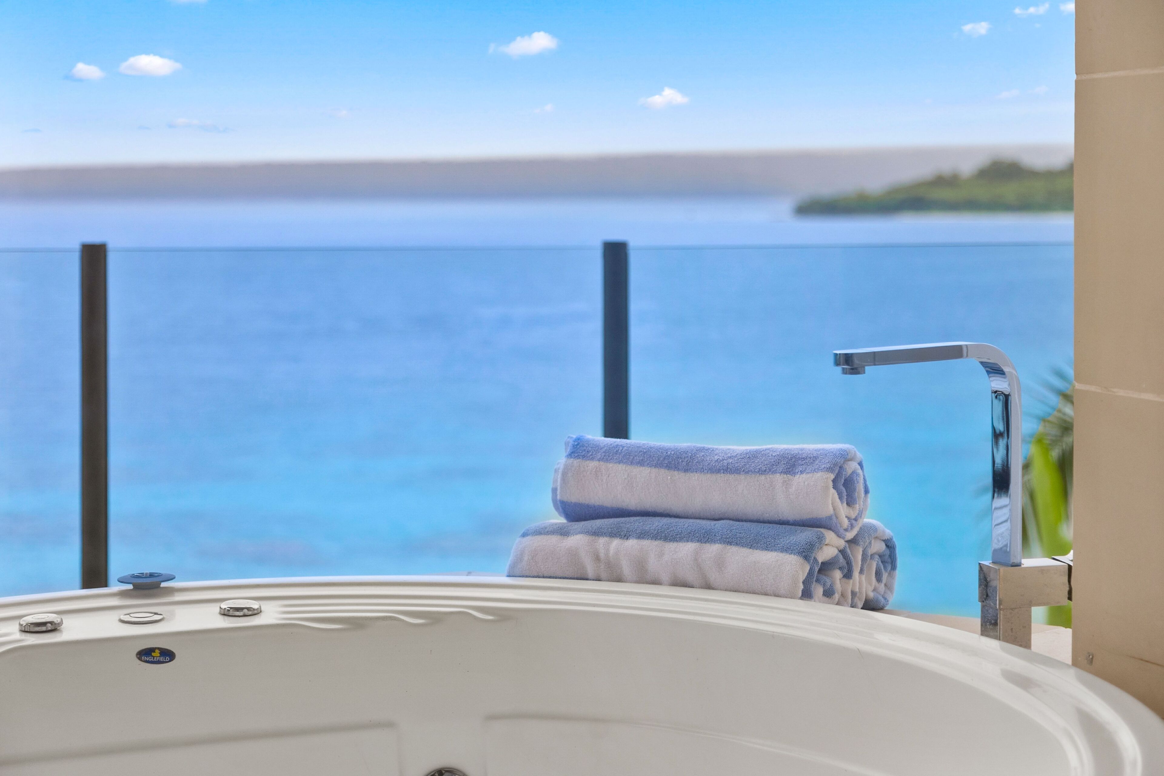 Um banheiro com banheira, porta-toalhas com toalhas e vista para o mar.