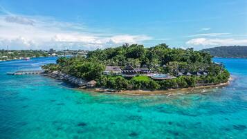 Um resort em ilha com bangalôs sobre a água, piscina e vegetação exuberante.