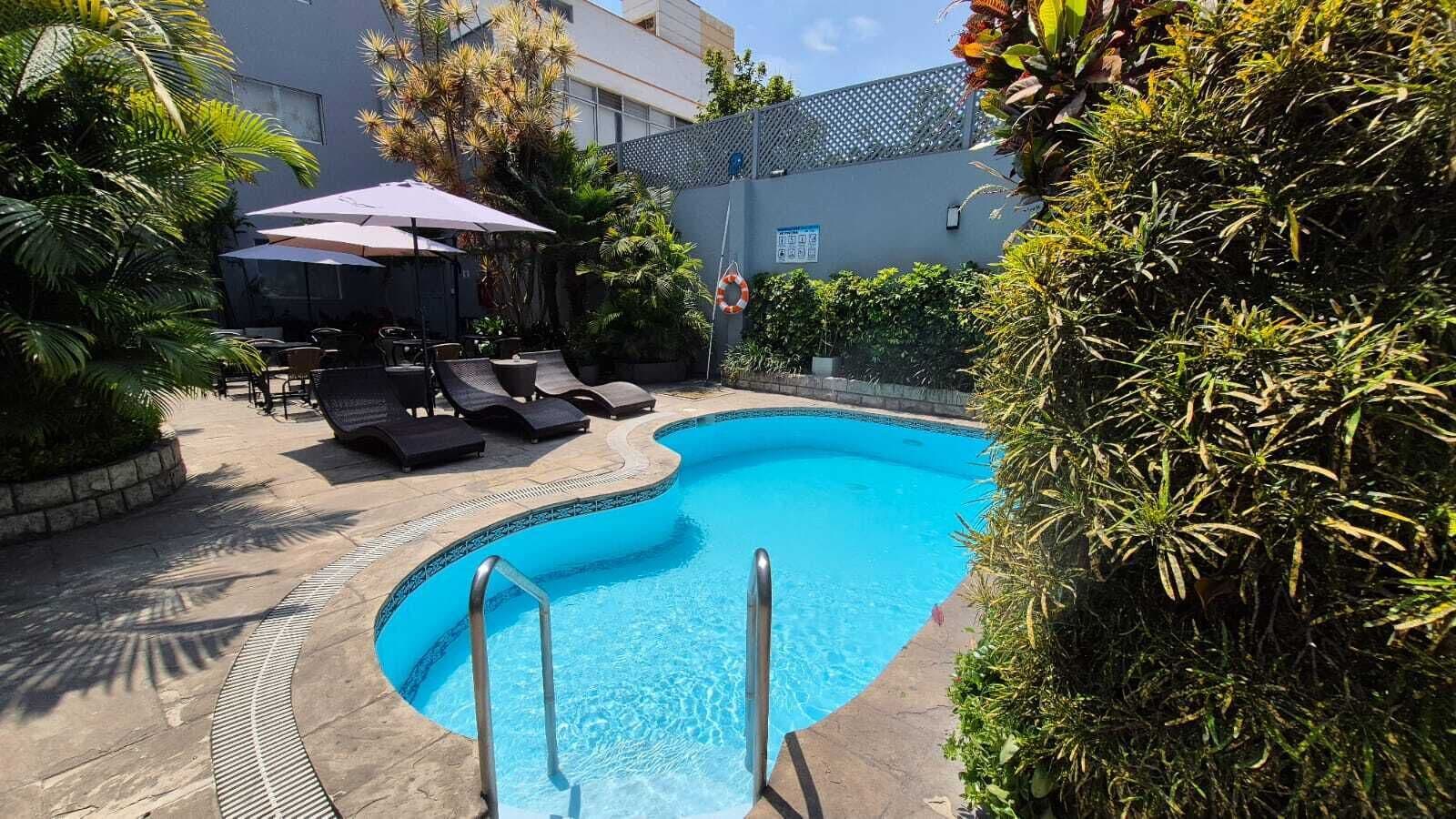 Piscina com borda curva, rodeada por espreguiçadeiras e guarda-sóis.