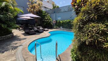 Piscina com borda curva, rodeada por espreguiçadeiras e guarda-sóis.