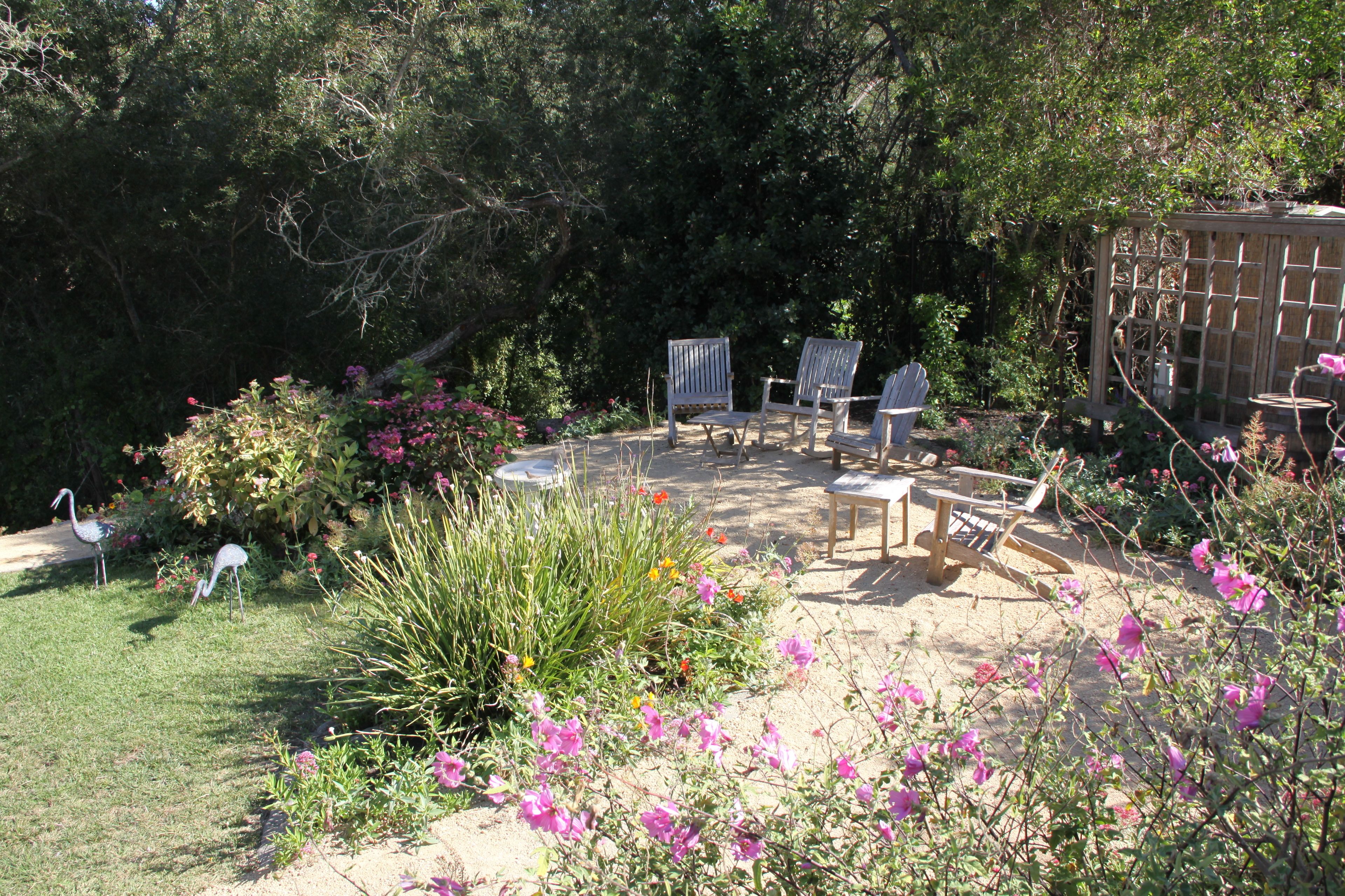 Um jardim com um deck de madeira, cadeiras e uma mesa.