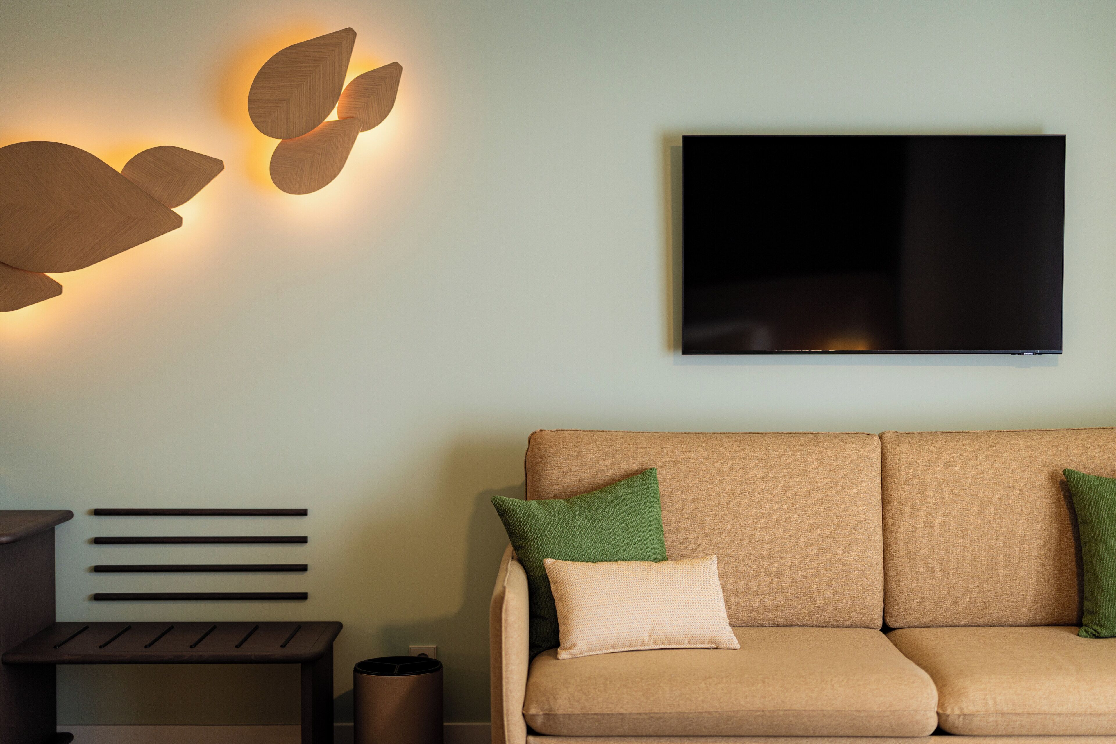 Uma sala de estar moderna com um sofá, uma TV de tela plana e um luminário fixado na parede.