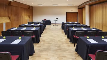Sala de conferências com mesas e cadeiras dispostas em fileiras, equipada com projetores e telas de projeção.