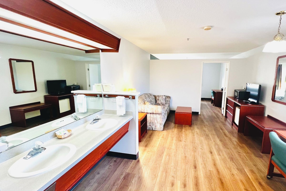 Quarto de hotel espaçoso com banheiro amplo, sofá, televisão e área de jantar.