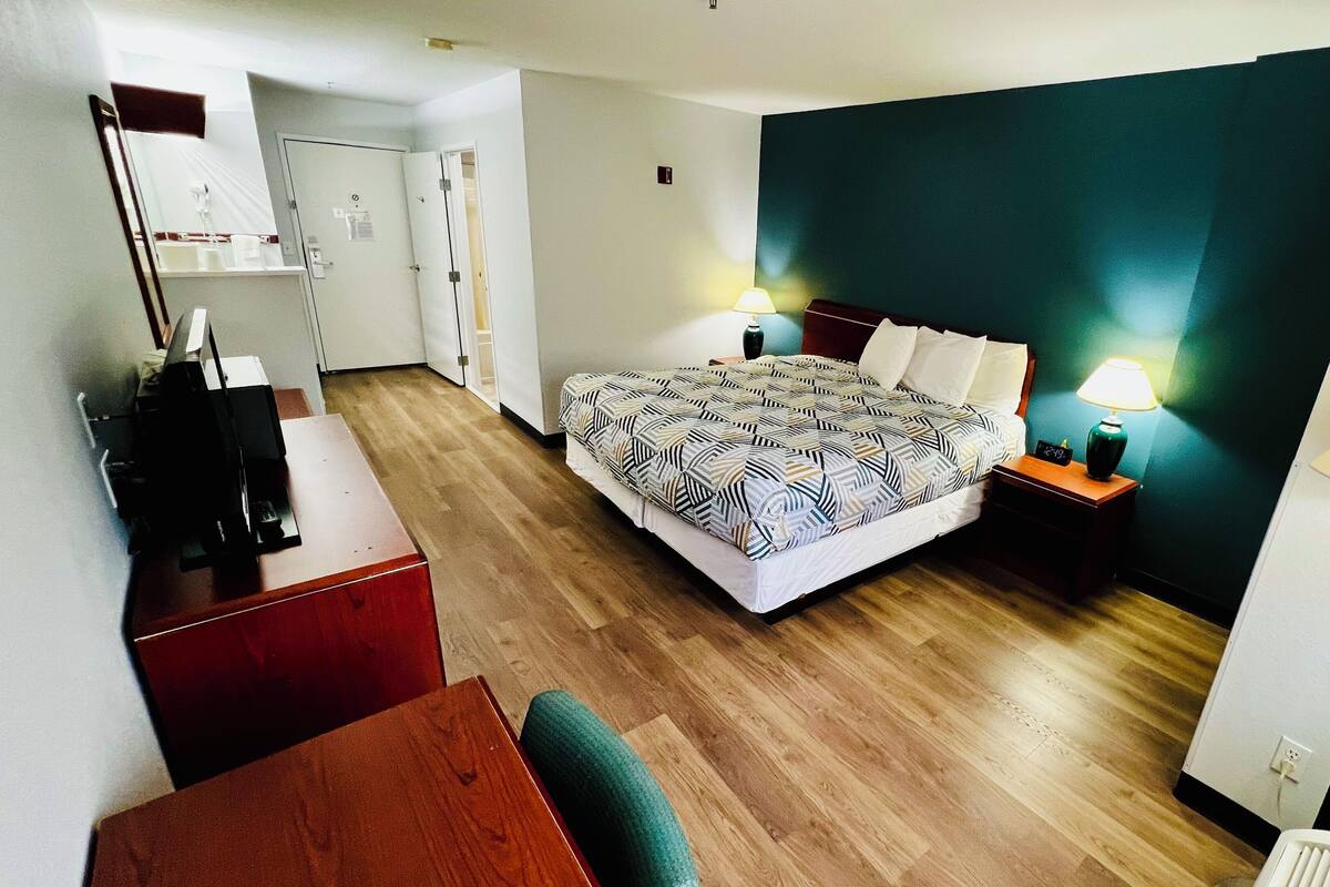 Quarto de hotel com uma cama, mesas de cabeceira, escrivaninha, cadeira e guarda-roupa.