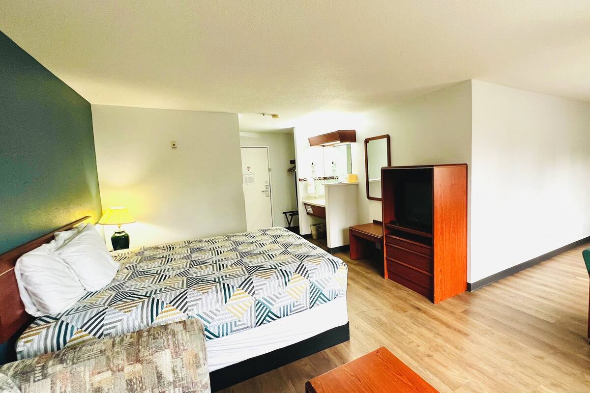 Quarto de hotel com cama, escrivaninha, cadeira, guarda-roupa e espelho.
