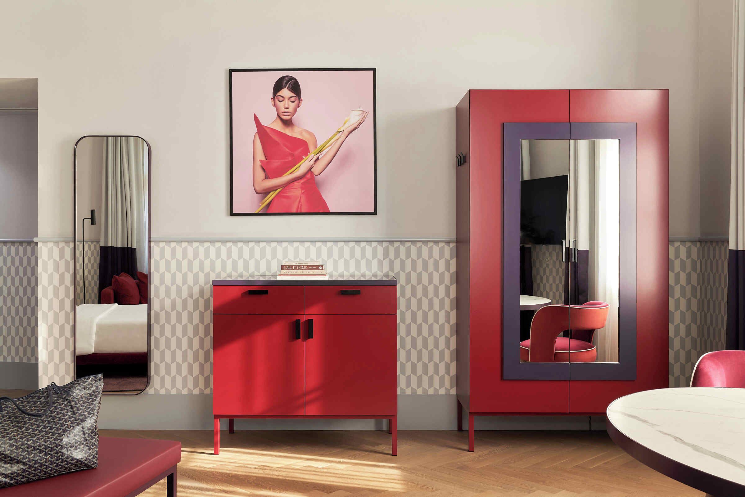 Quarto moderno com um guarda-roupa vermelho, um espelho grande, uma obra de arte emoldurada e um espaço de refeições com uma mesa redonda.