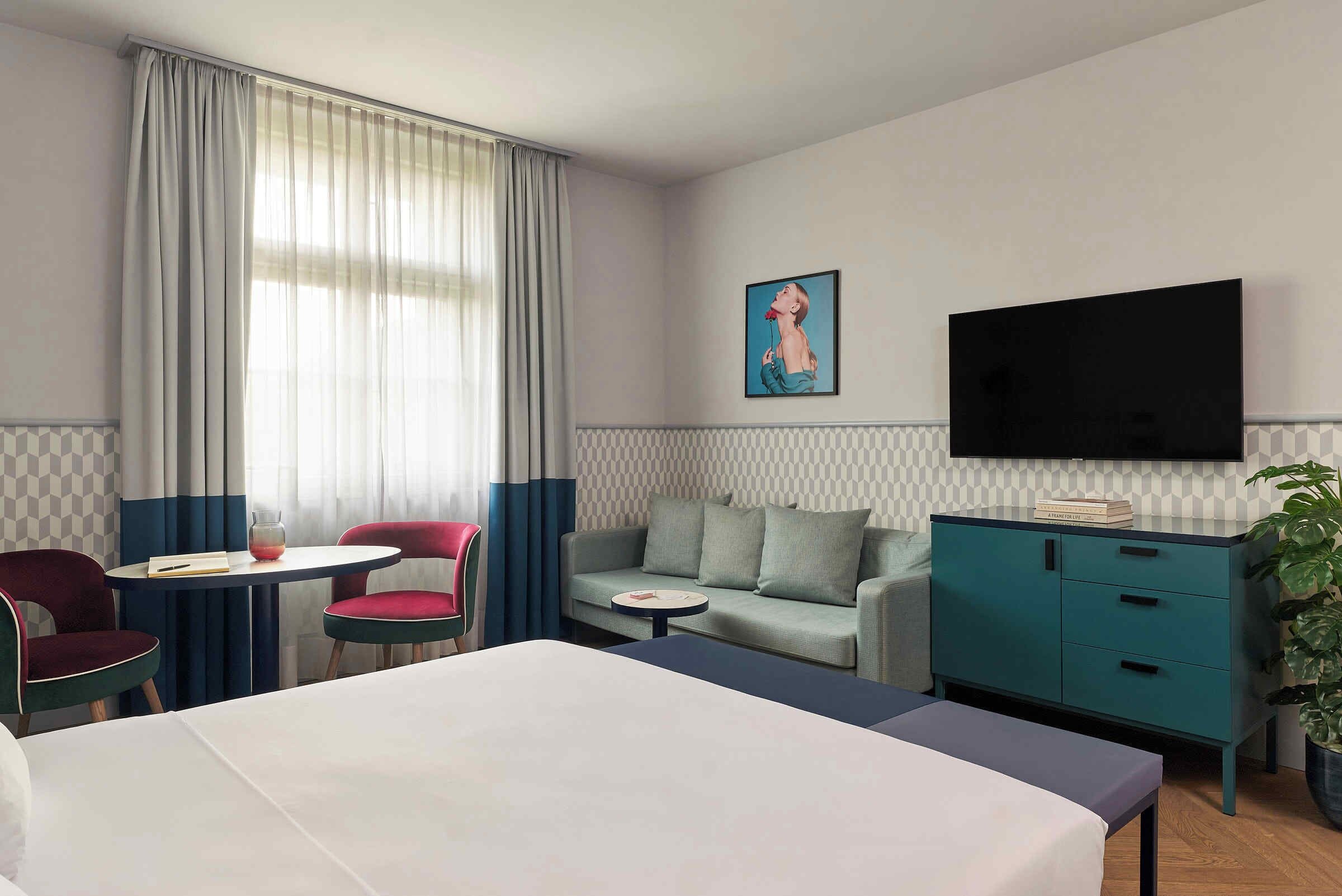 Quarto de hotel com cama, sofá, televisão, mesa pequena e cadeira.
