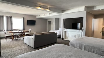 Quarto de hotel com duas camas, um sofá, uma mesa de jantar com cadeiras, uma televisão e uma kitchenette.