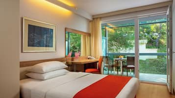 Quarto de hotel com cama, escrivaninha, cadeira e varanda com vista para o verde.
