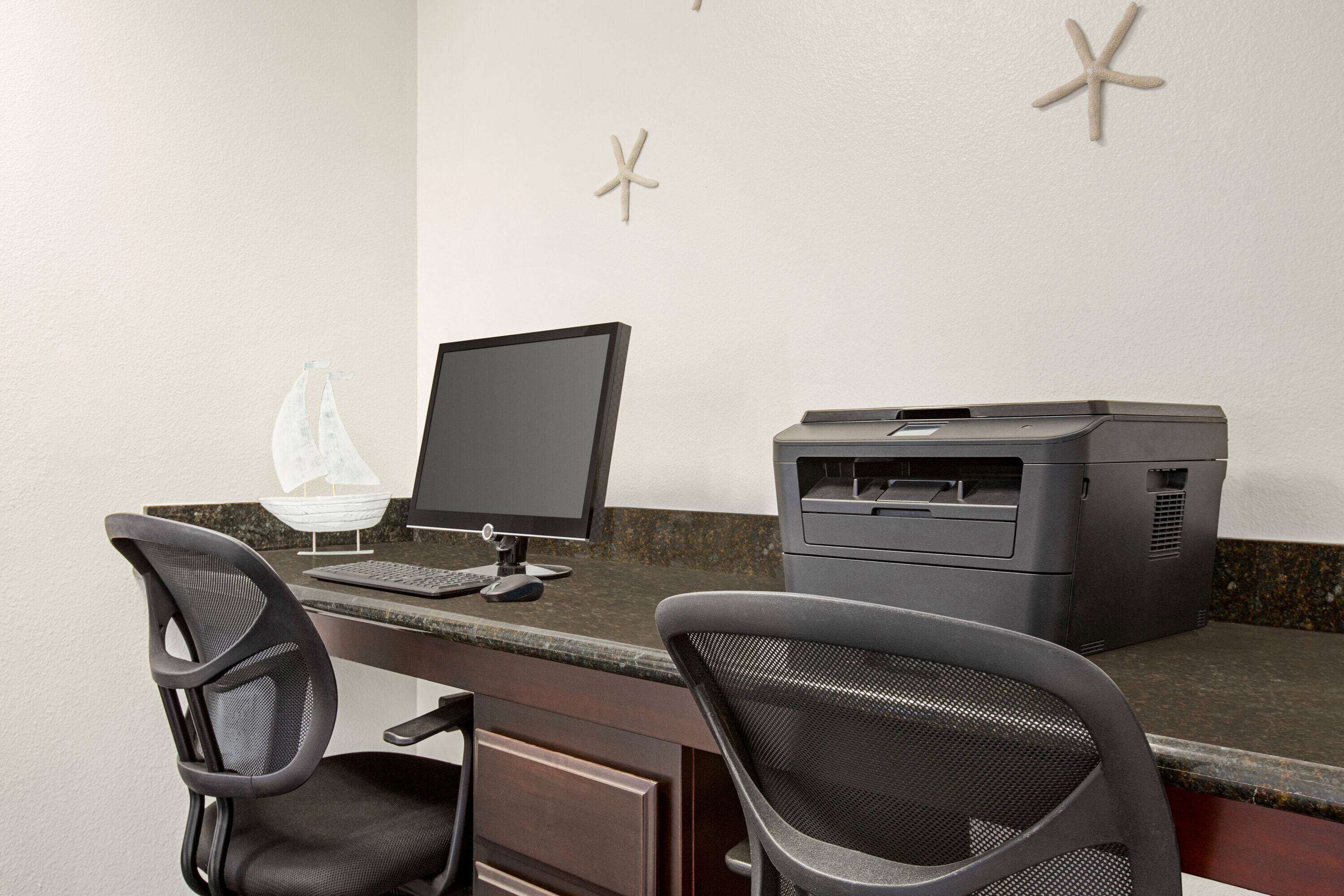 Um espaço de trabalho com duas cadeiras, uma mesa, um monitor de computador e uma impressora.