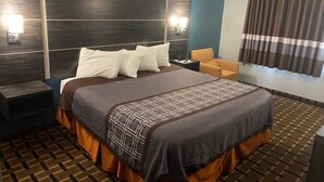 Quarto de hotel com uma cama grande, duas mesas de cabeceira, uma luminária e uma cadeira, além de uma janela com cortinas.