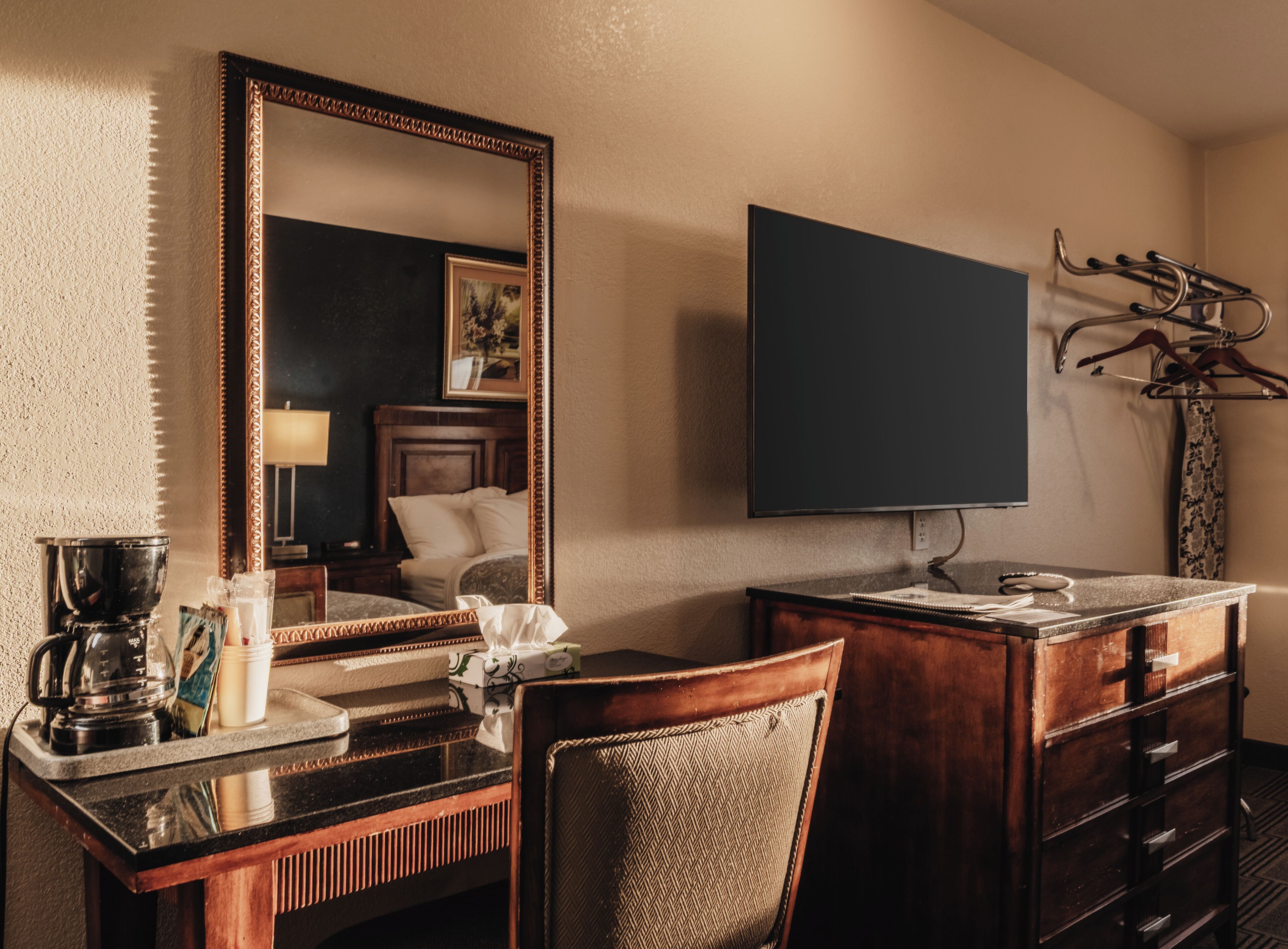Quarto de hotel com uma secretária de madeira, uma cadeira, um espelho grande, televisão de tela plana e um porta-roupas.