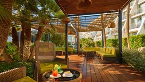 Um pátio externo com mobiliário de vime, uma mesa com bebidas e vista para um edifício moderno.