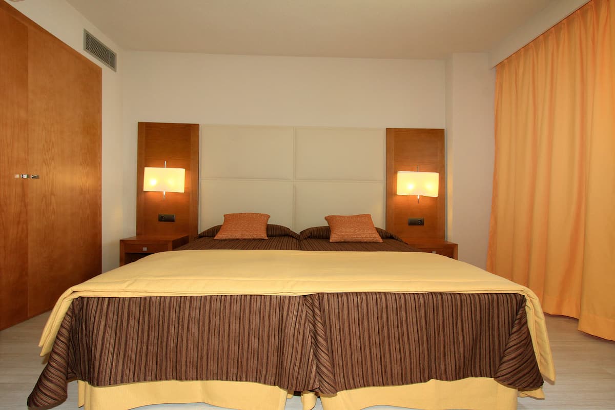 Quarto de hotel com uma cama grande, duas mesas de cabeceira com luminárias e um guarda-roupa de madeira.