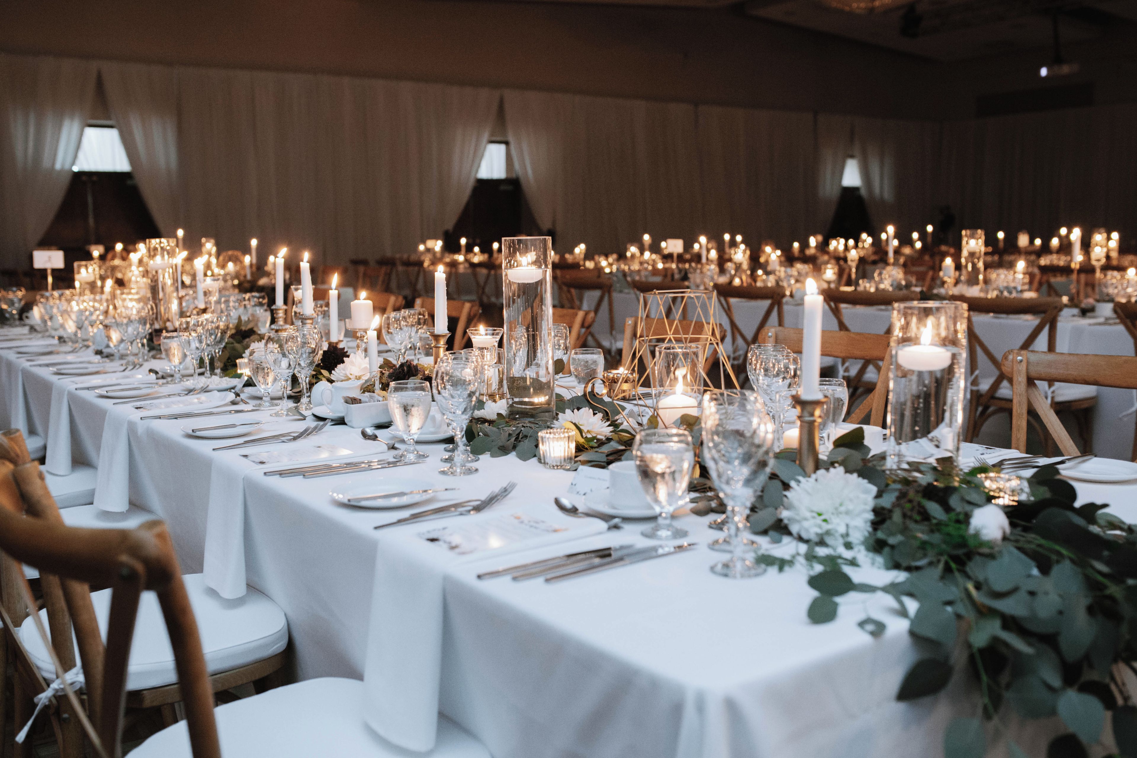 Uma longa mesa de banquete montada para um evento formal, com várias velas, copos e elegantes louças.