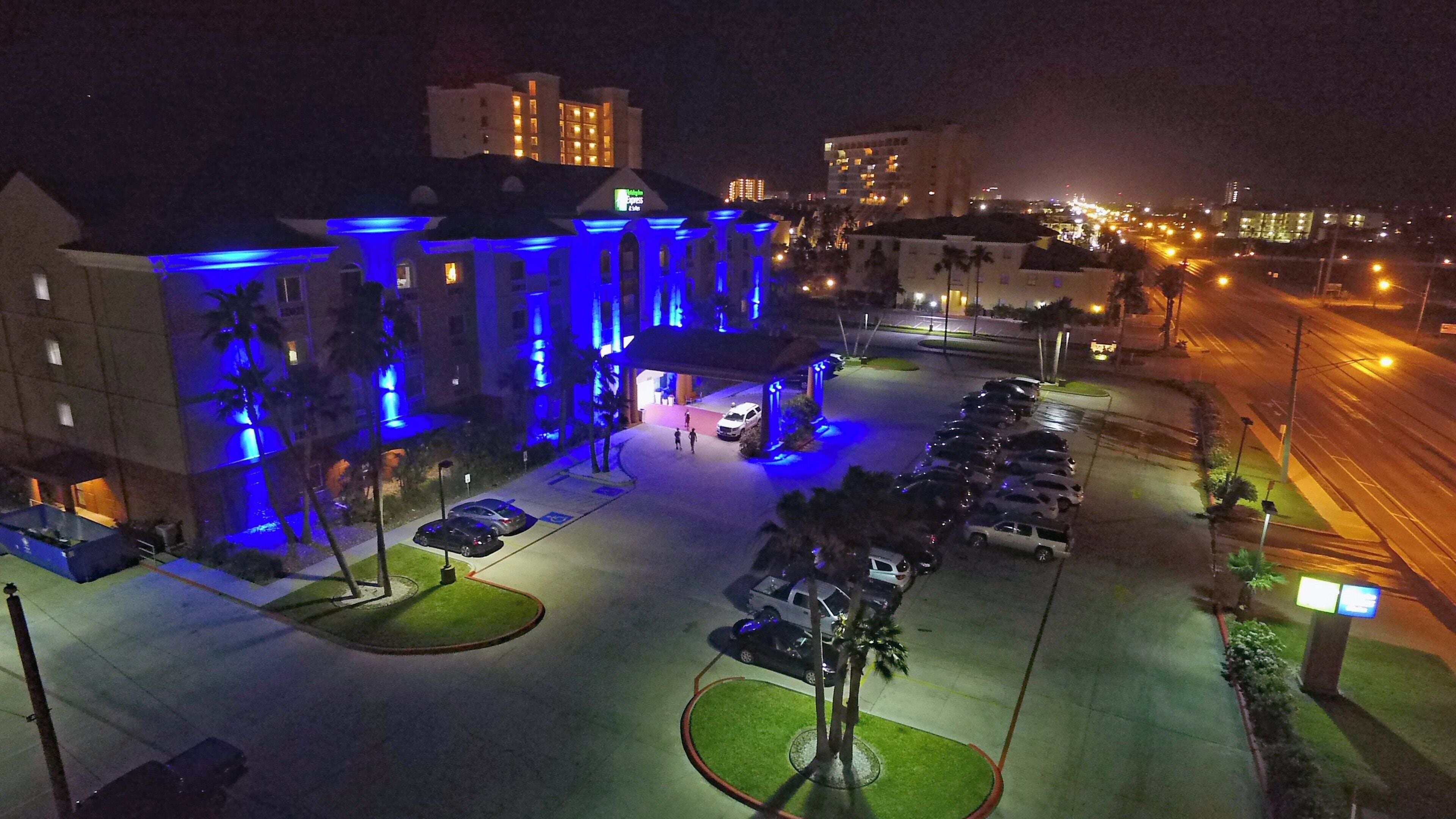 Hotel com estacionamento, entrada coberta e fachada iluminada com luzes azuis.