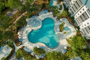 Vista aérea de um resort com uma piscina central, rodeada por áreas de descanso e palmeiras.