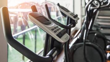 Uma bicicleta ergométrica com visor digital e painel de controle, parte de uma academia com equipamentos de ginástica.