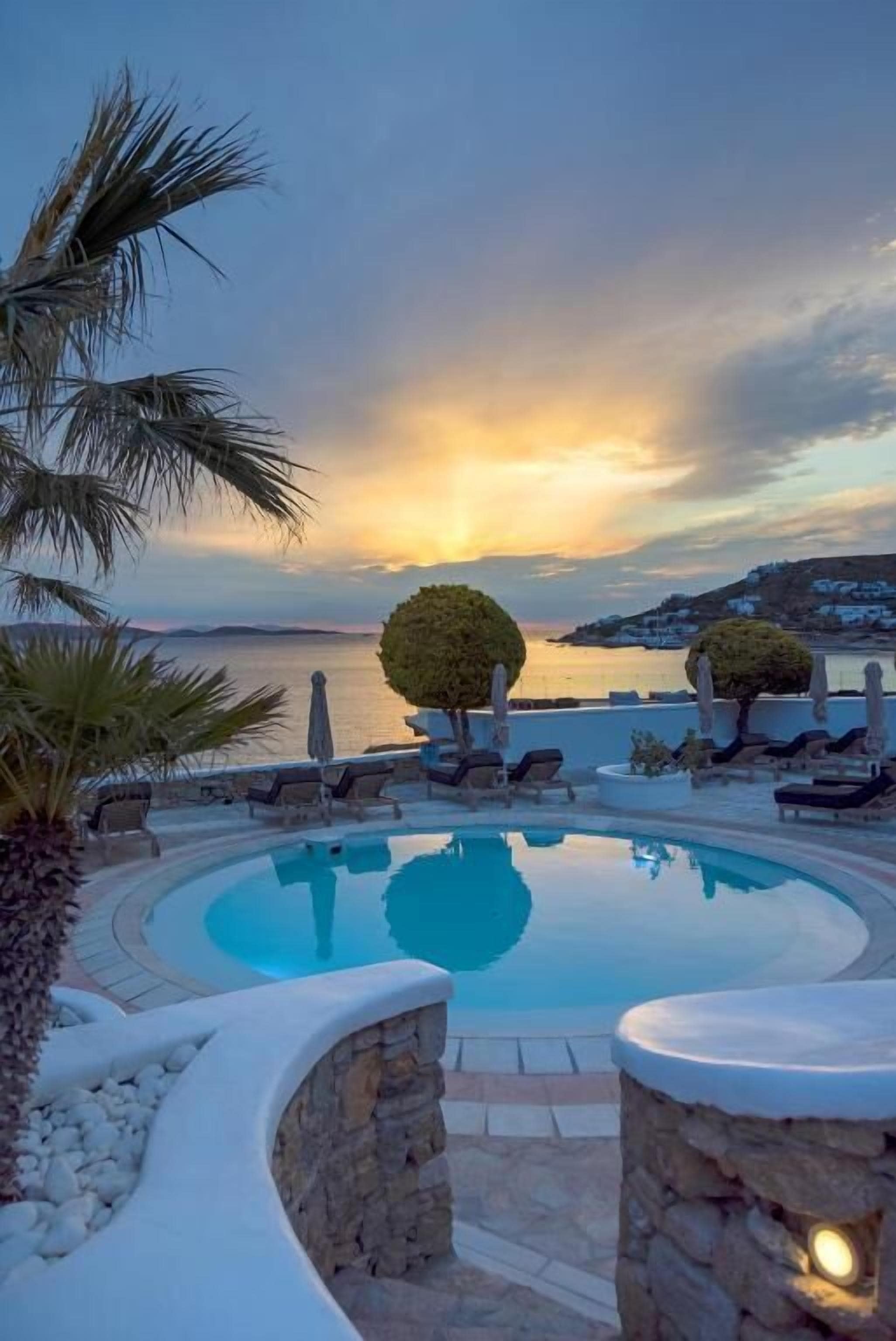 Área da piscina com espreguiçadeiras e vista para o mar ao pôr do sol.
