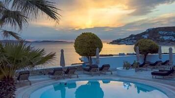 Área da piscina com espreguiçadeiras e vista para o mar ao pôr do sol.
