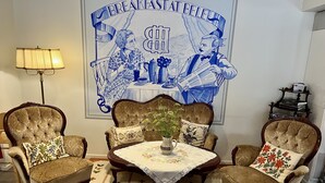 Quarto com duas poltronas, uma mesinha de centro com toalha de renda, um abajur e um pôster grande na parede.