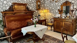 Quarto em estilo vintage com um sofá de madeira, uma mesa com toalha rendada, um tapete estampado com flores, um armário de madeira e um candelabro.