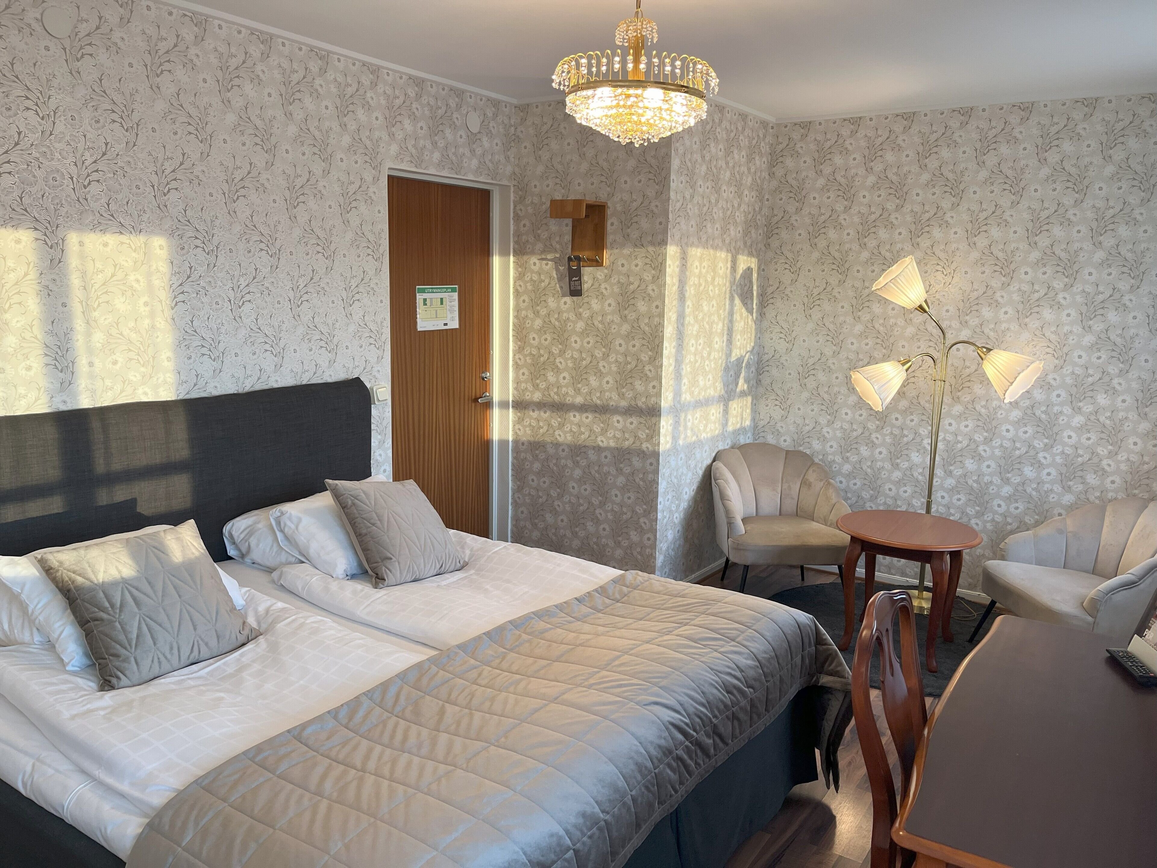 Quarto de hotel com uma cama grande, escrivaninha, cadeira e lustre.