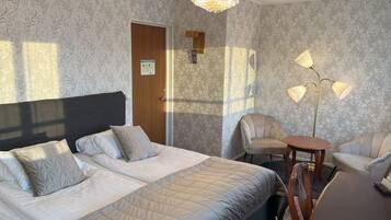 Quarto de hotel com uma cama grande, escrivaninha, cadeira e lustre.
