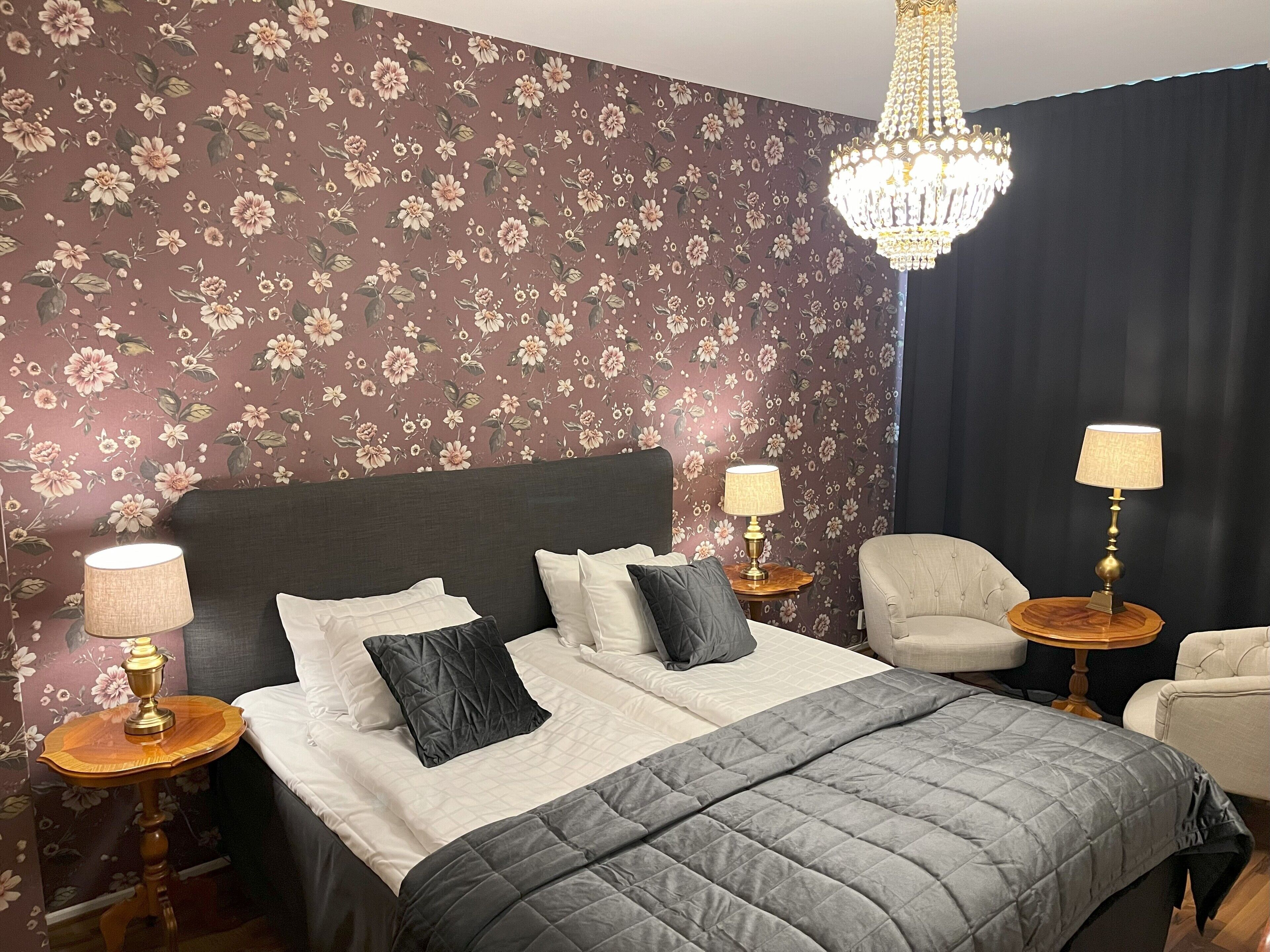 Quarto com uma cama grande, duas mesas de cabeceira com luminárias, um candelabro e uma cadeira.