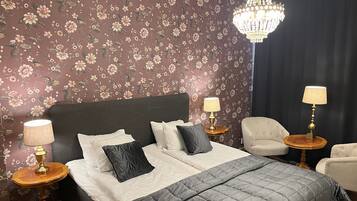 Quarto com uma cama grande, duas mesas de cabeceira com luminárias, um candelabro e uma cadeira.