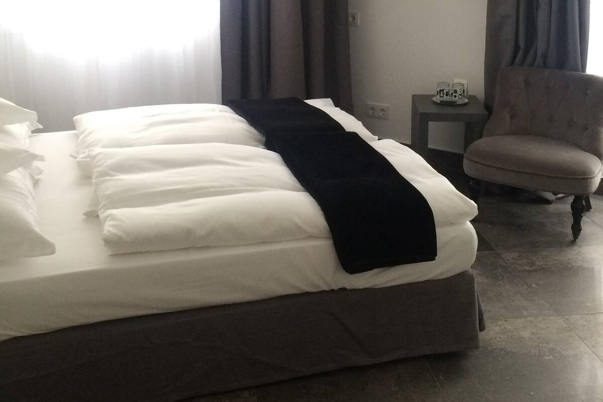 Quarto de hotel com cama, uma cadeira, uma mesinha e uma televisão de tela plana presa na parede.