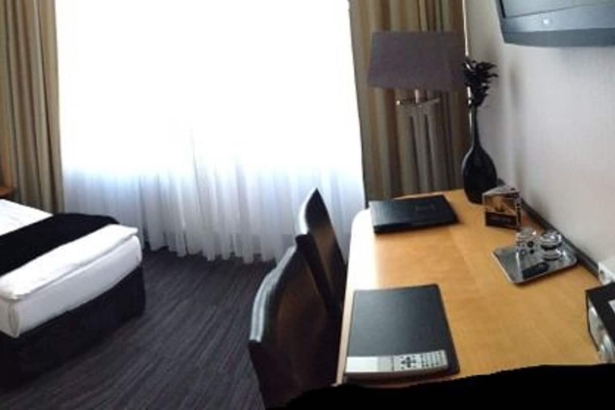 Quarto de hotel com duas camas, uma escrivaninha com um laptop, uma cadeira, um abajur e uma televisão.
