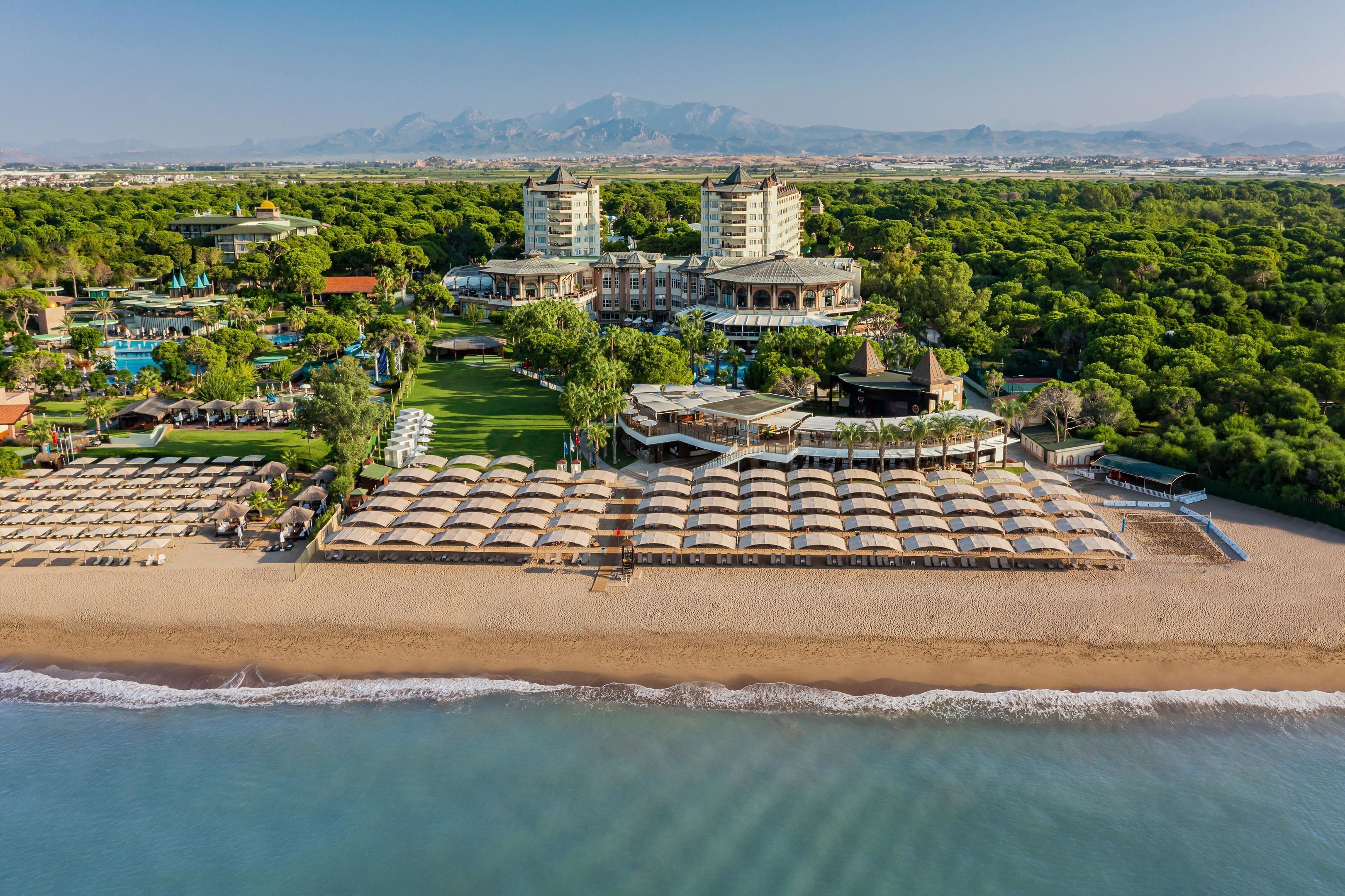 Um resort com praia, vários edifícios e montanhas ao fundo.