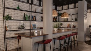 Uma cozinha moderna com uma ilha central, banquetas de bar, prateleiras com garrafas e plantas, e um lustre.