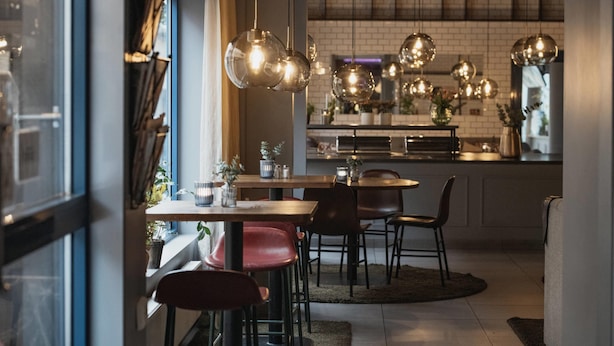 Cozinha moderna com luminárias pendentes, área de jantar com cadeiras e vista através de uma porta de vidro.