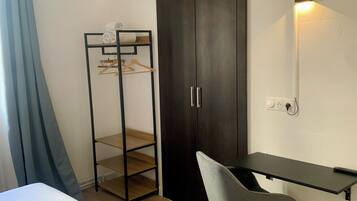 Quarto com cama, escrivaninha com cadeira, guarda-roupa e prateleira suspensa com roupas.