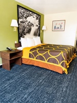 Quarto de hotel com cama, duas luminárias, telefone, escrivaninha e um quadro na parede.