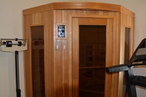 Uma sauna de madeira com um painel de controle, uma cadeira preta e um dispositivo de medição na parede.