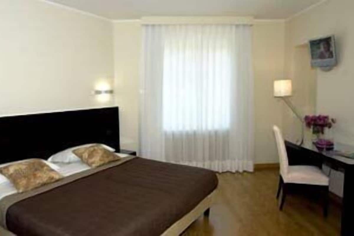 Quarto de hotel com uma cama, uma escrivaninha e uma cadeira.