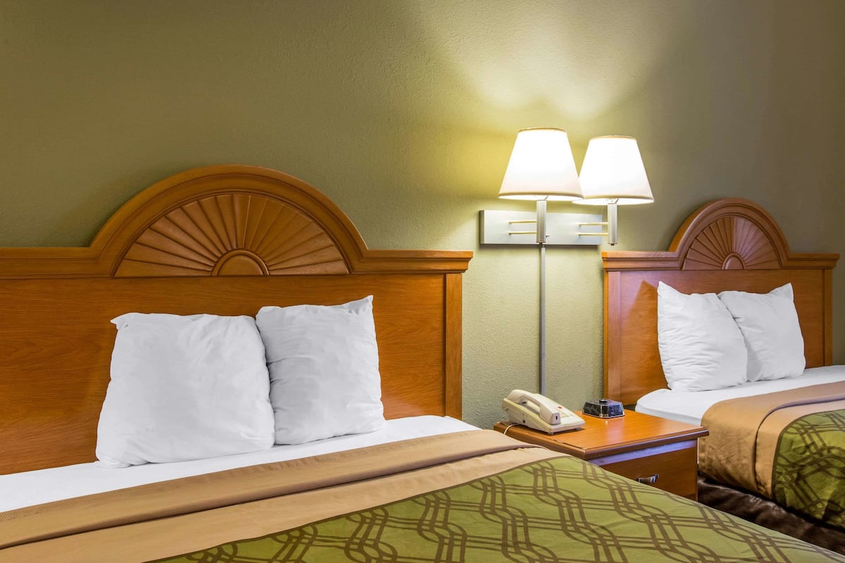 Quarto de hotel com duas camas, abajur, telefone e interruptor de luz na parede.
