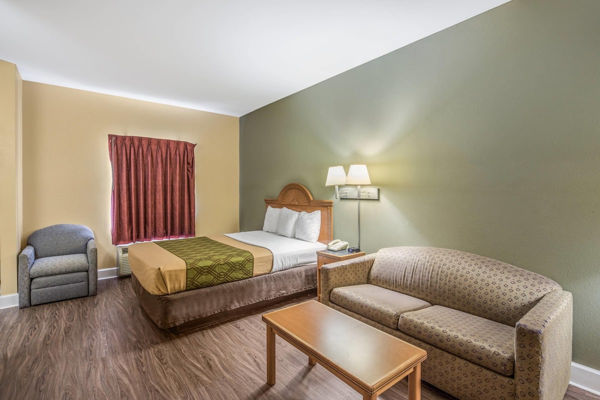 Quarto de hotel com cama, sofá, cadeira, mesa, abajur e telefone.