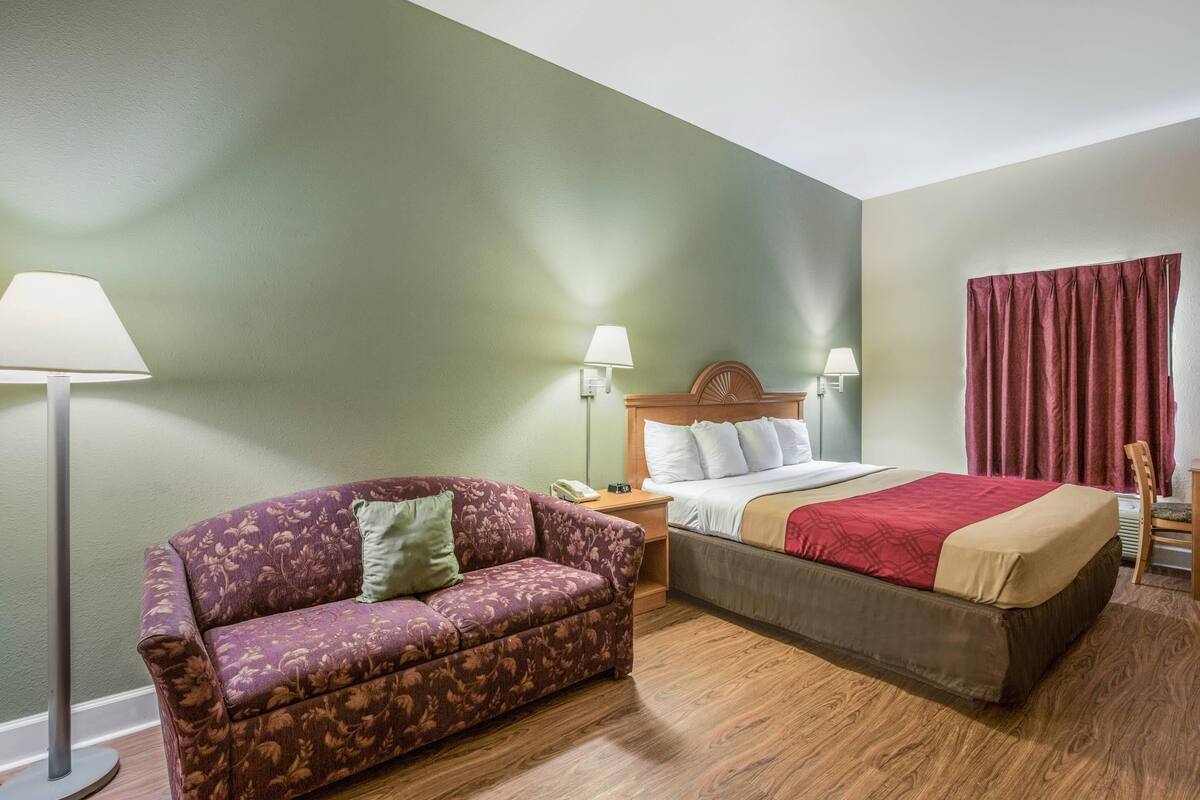 Quarto de hotel com cama, sofá, mesa de cabeceira e luminária.