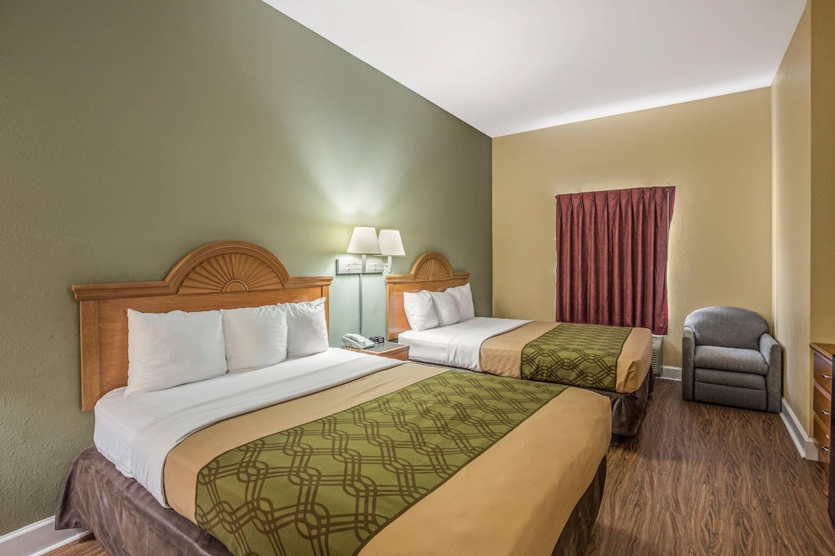Quarto de hotel com duas camas, uma cadeira, uma mesa de cabeceira e um abajur.