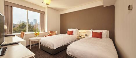 Quarto de hotel com duas camas, uma escrivaninha, uma cadeira, uma mesinha com um vaso e uma janela com cortinas.