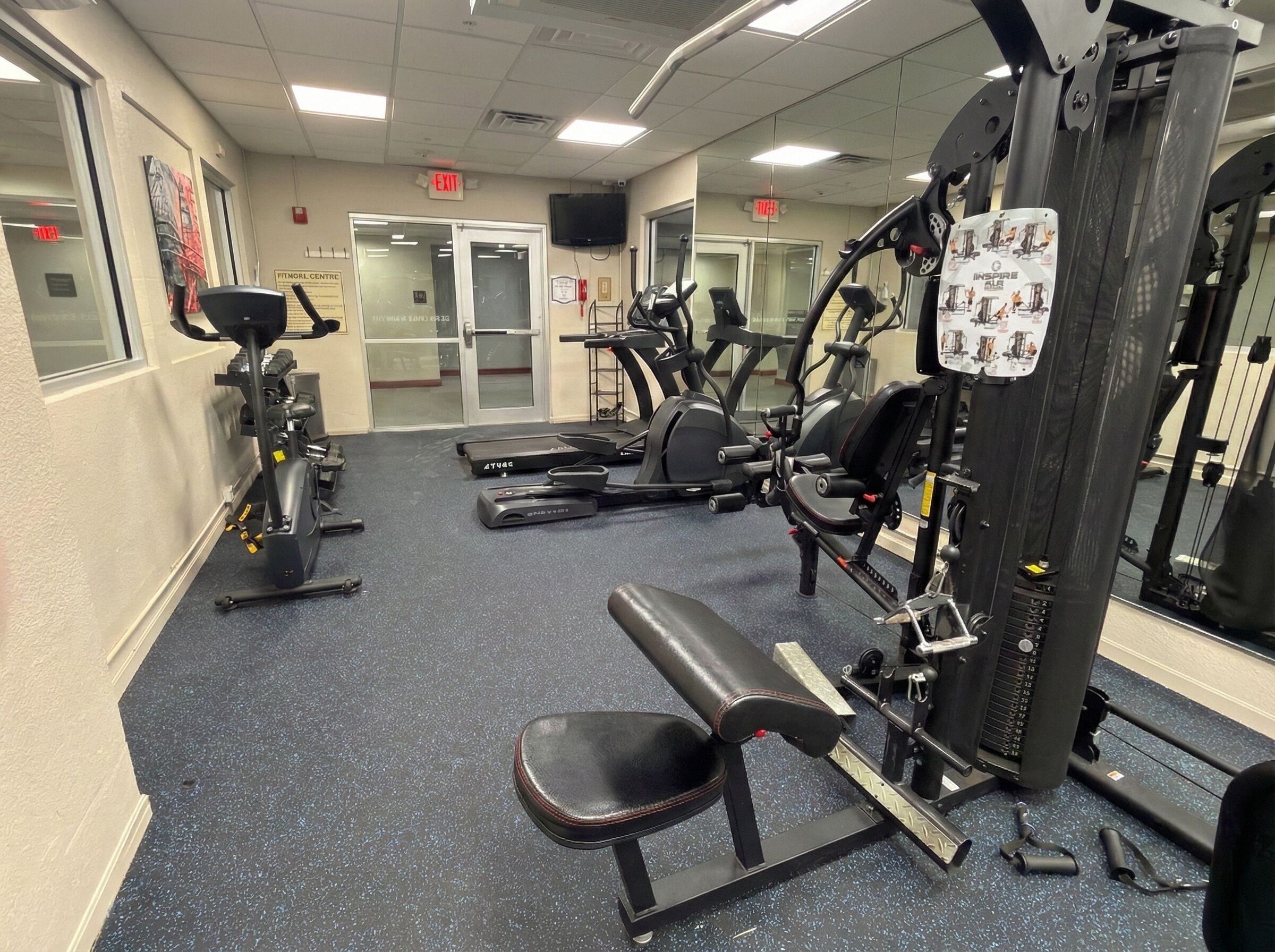Uma academia com diversos equipamentos de exercício, incluindo esteiras, um banco e máquinas de musculação.