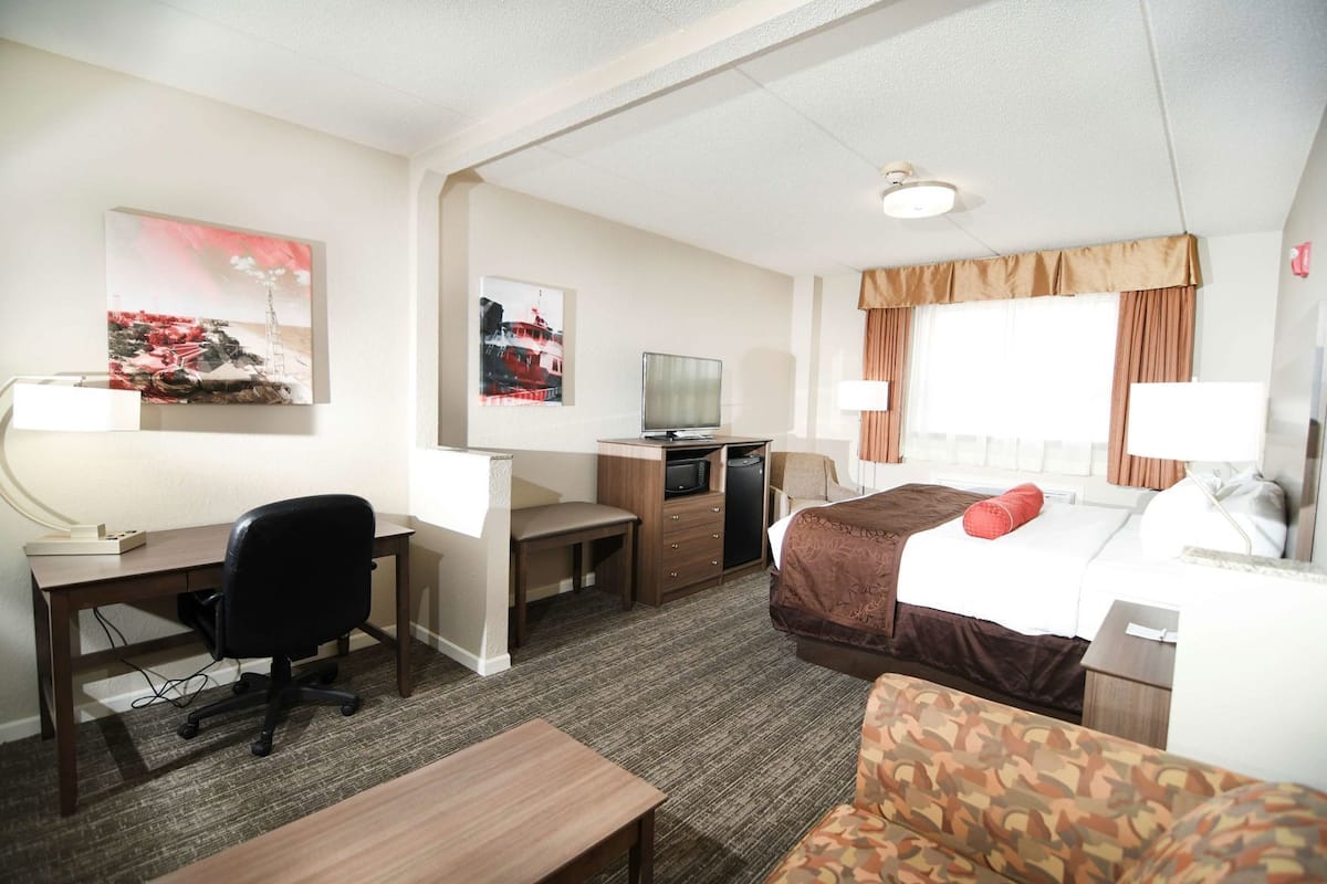 Quarto de hotel com cama, escrivaninha, cadeira, televisão e obras de arte nas paredes.