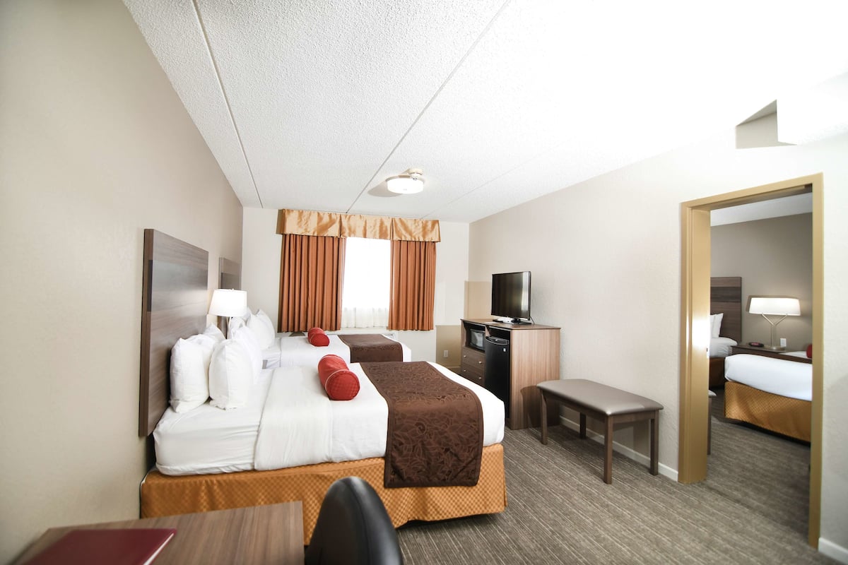 Quarto de hotel com duas camas, uma escrivaninha, uma televisão e um espelho.