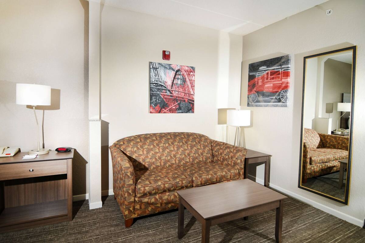 Quarto de hotel com sofá, uma mesa pequena, escrivaninha com abajur e duas pinturas penduradas na parede.